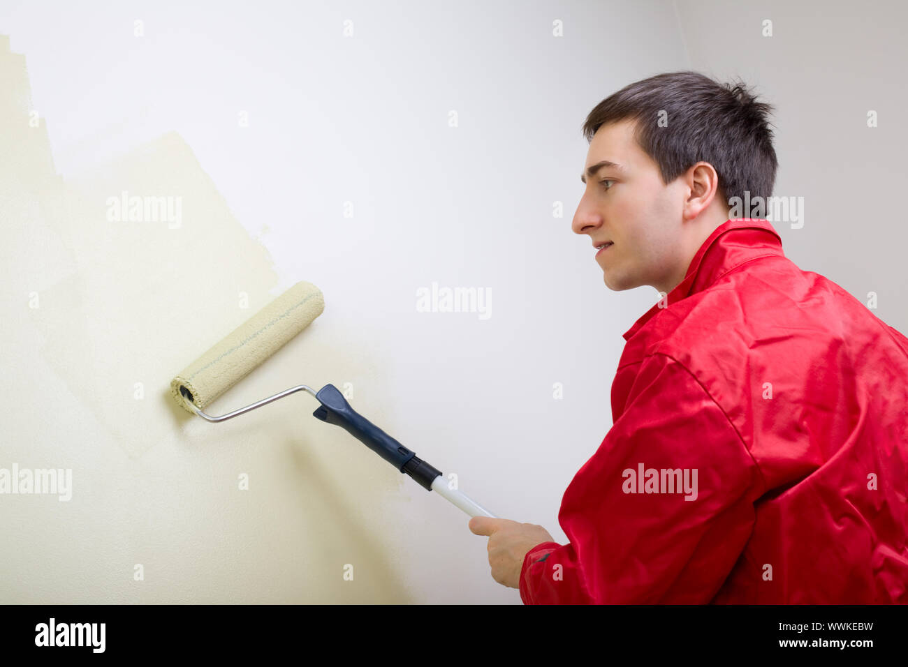 Man painting a wall. Painter in red overall painting wall in light ...