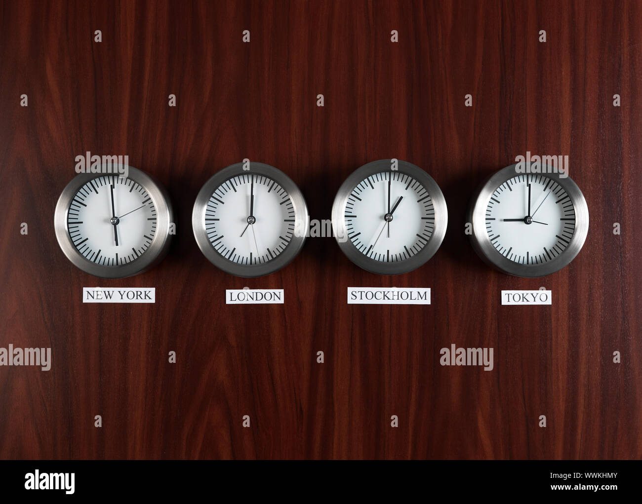 Four clocks with different time on Teak background Stock Photo - Alamy