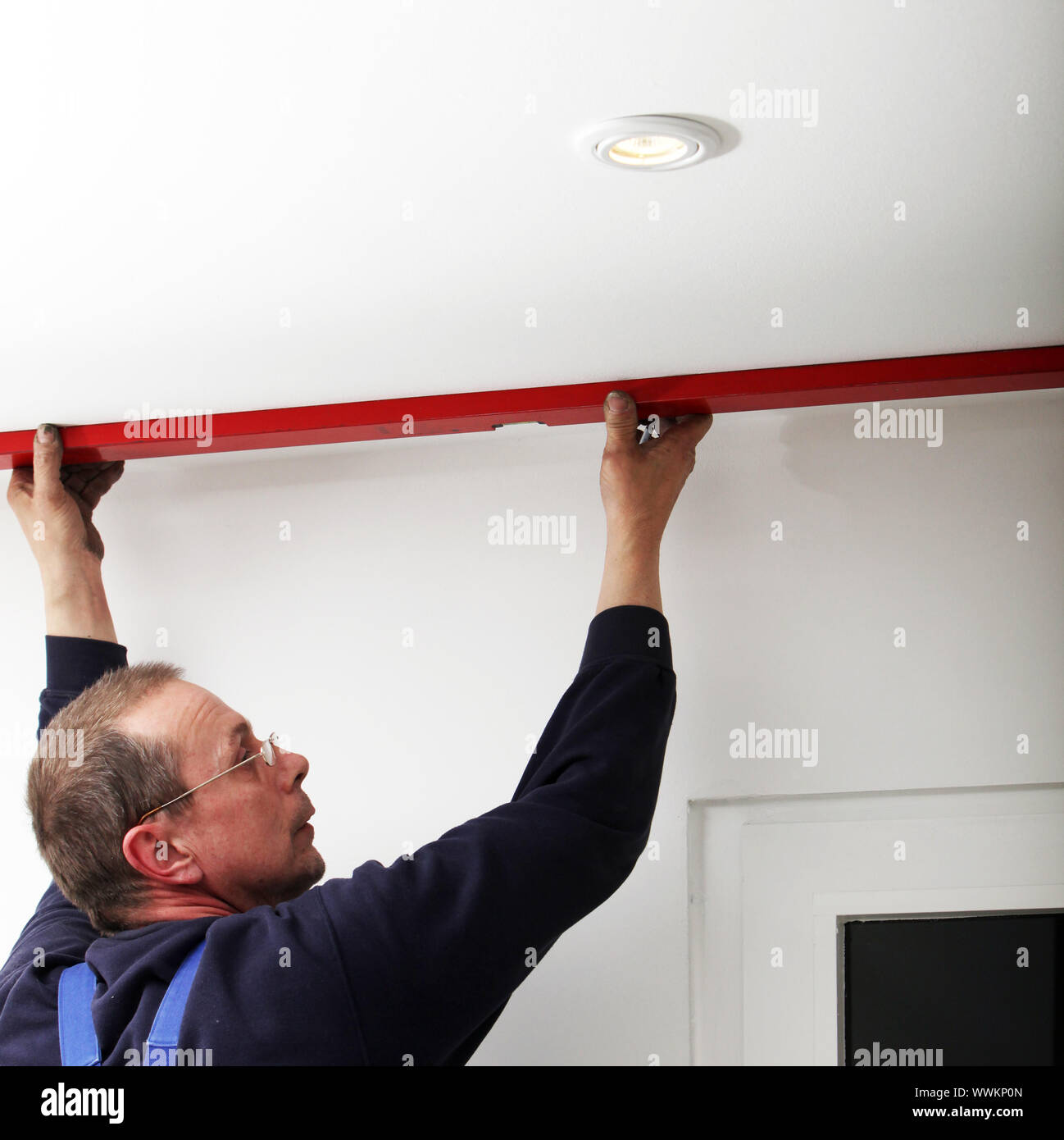 A middle-aged man uses a red spirit level to test that the ceiling is ...