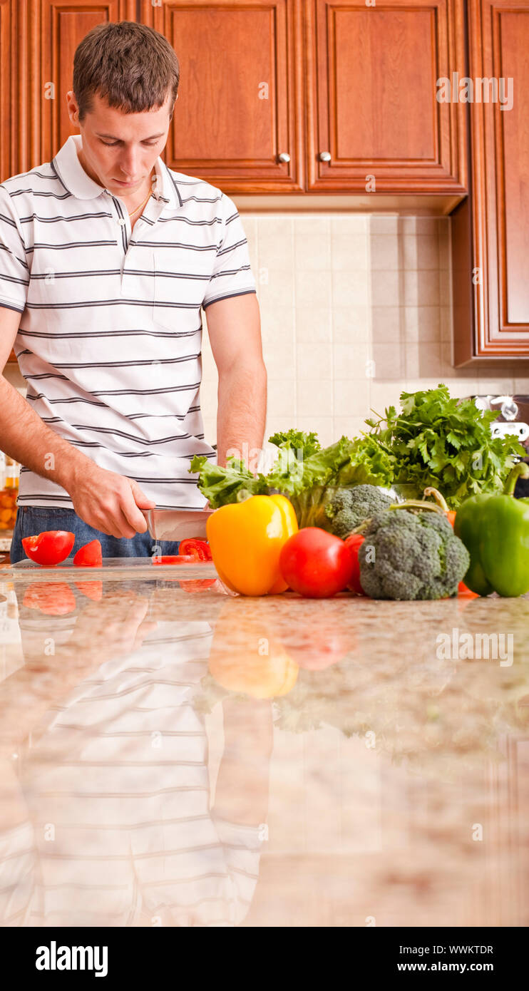 Young man cutting up tomato in kitchen for meal. Vertical shot Stock ...