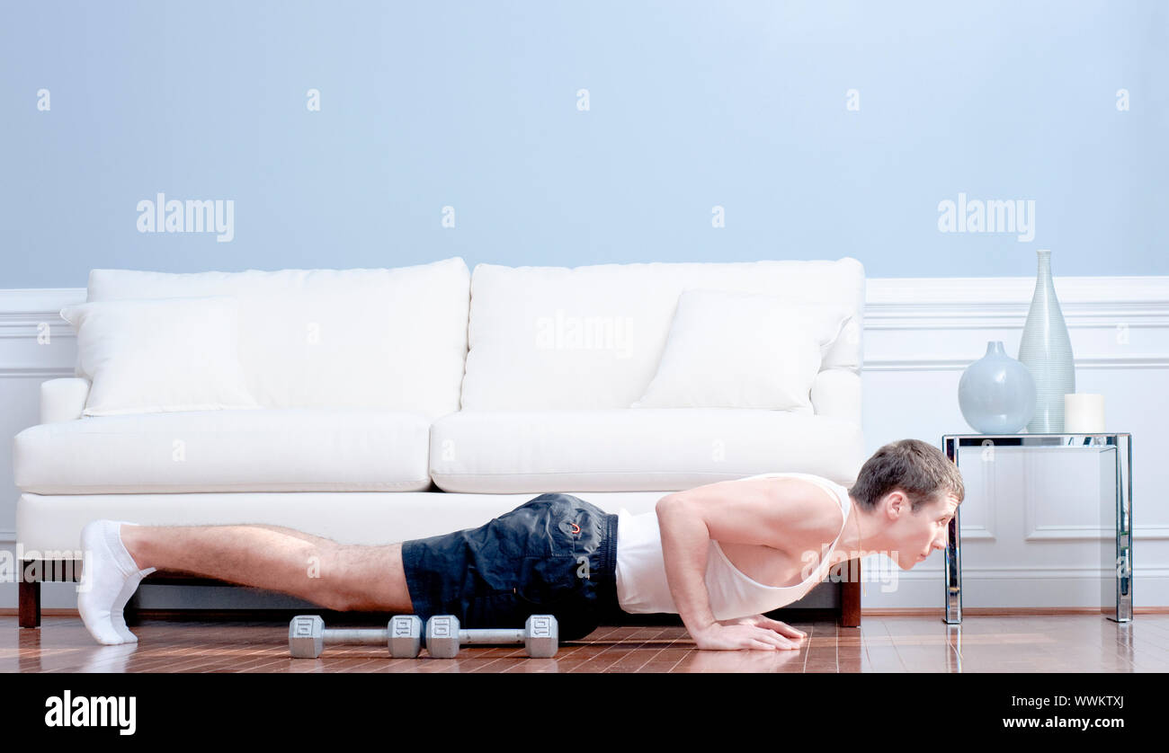 Full length view of man doing push-ups next to couch, with arm weights ...