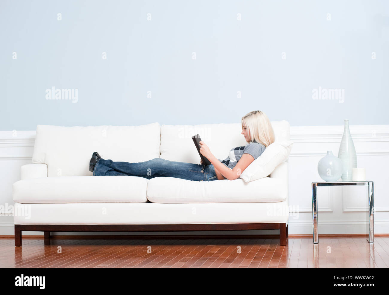 Full length view of woman reclining on white couch and reading a book ...