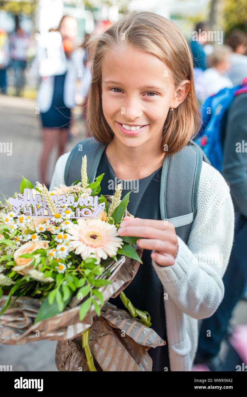 Adorable smilling girl with flowers posing in front of school. Adorable ...