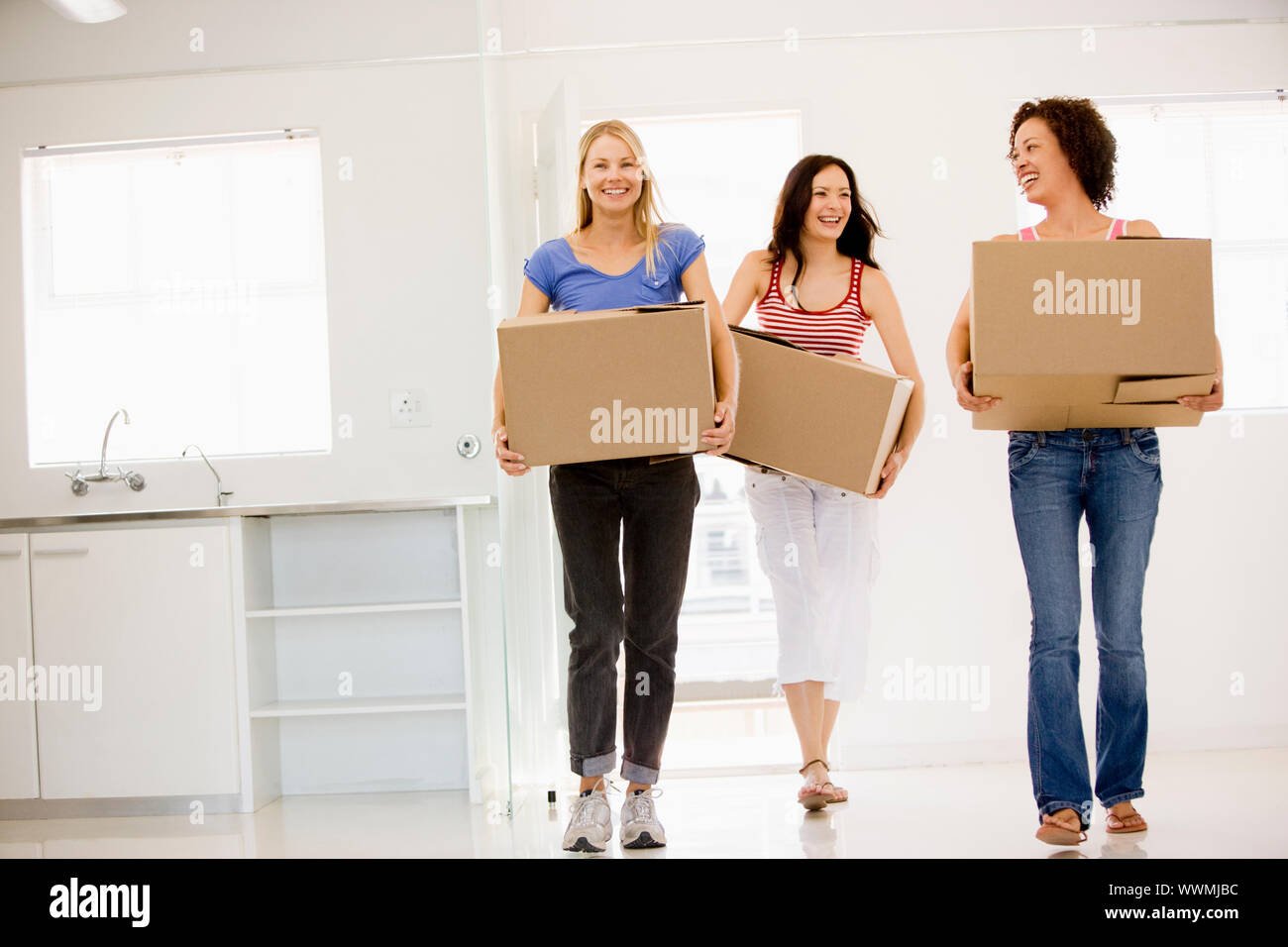 Three girl friends moving into new home smiling Stock Photo - Alamy