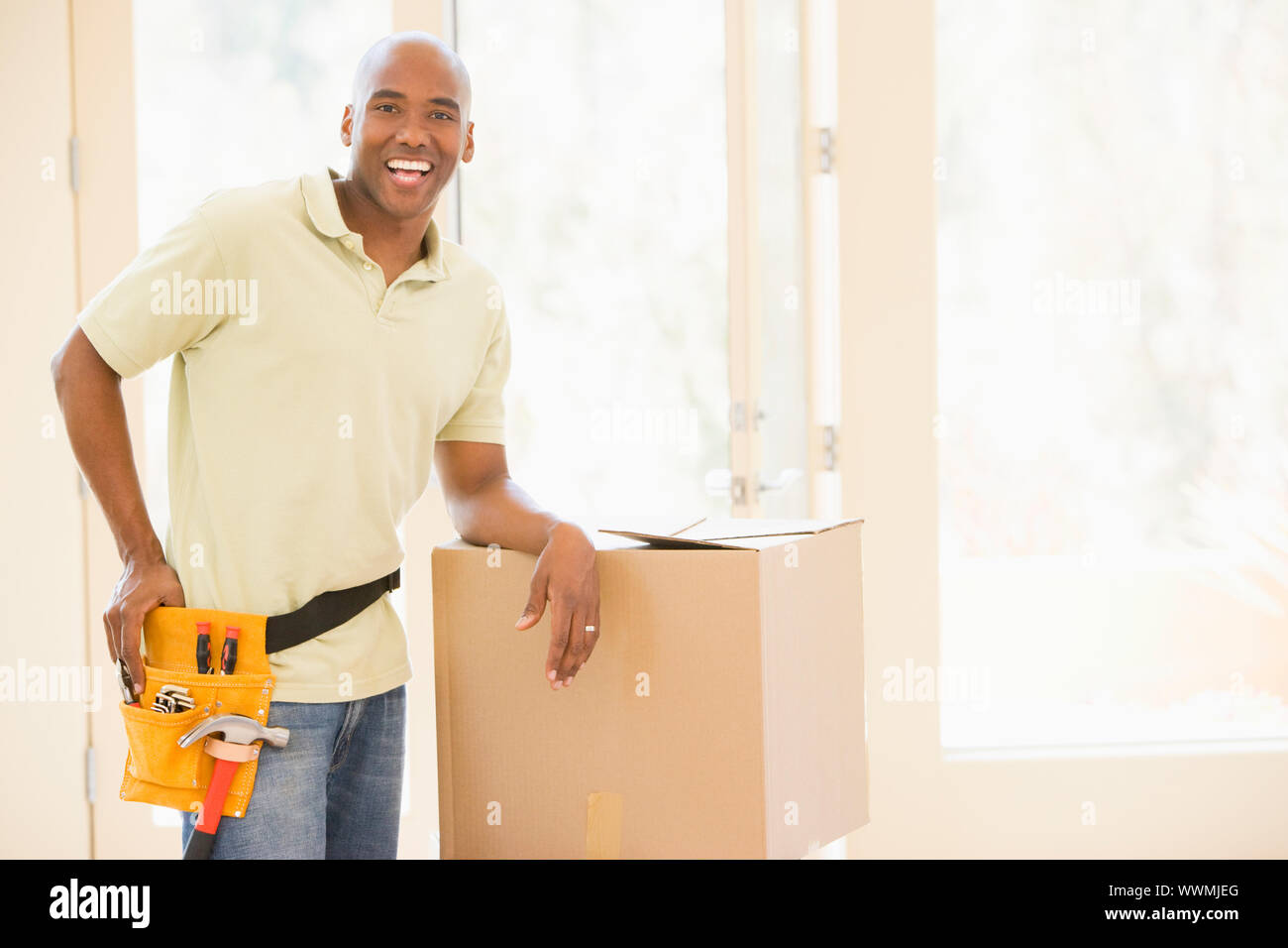 Man wearing tool belt standing by boxes in new home smiling Stock Photo ...