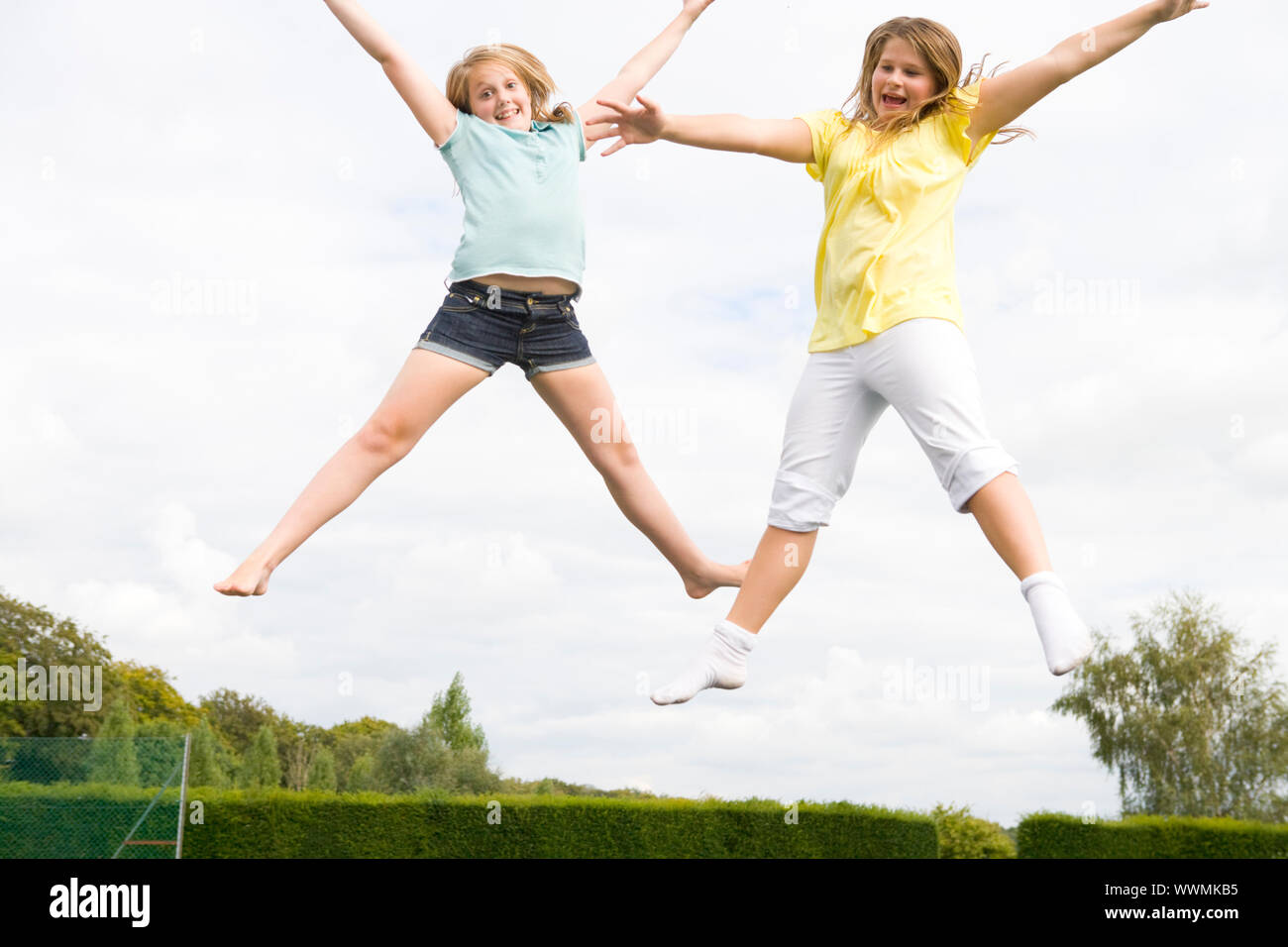 Two young girls jumping on trampoline smiling Stock Photo - Alamy