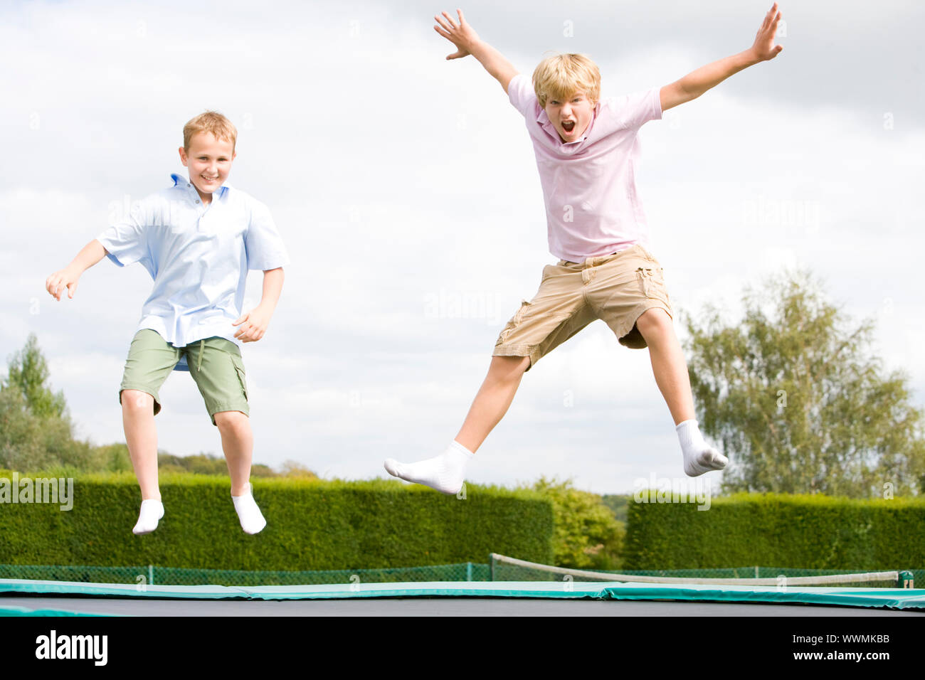 Two young boys jumping on trampoline smiling Stock Photo - Alamy