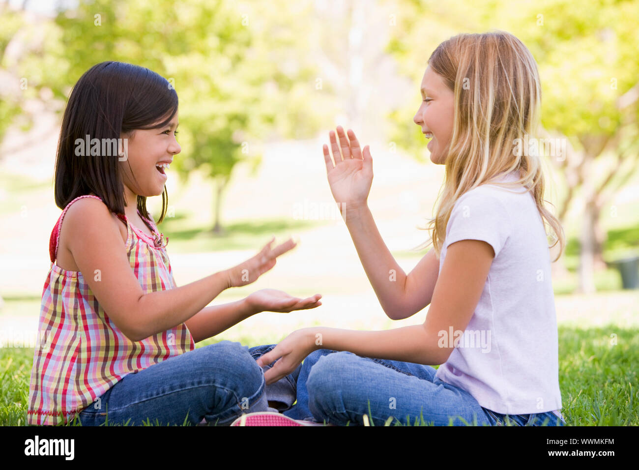 Two young girl friends sitting outdoors playing patty cake Stock Photo ...