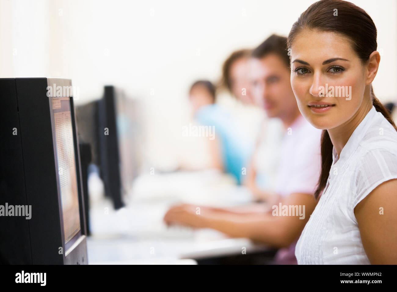 Woman sitting in computer room with people in background Stock Photo ...
