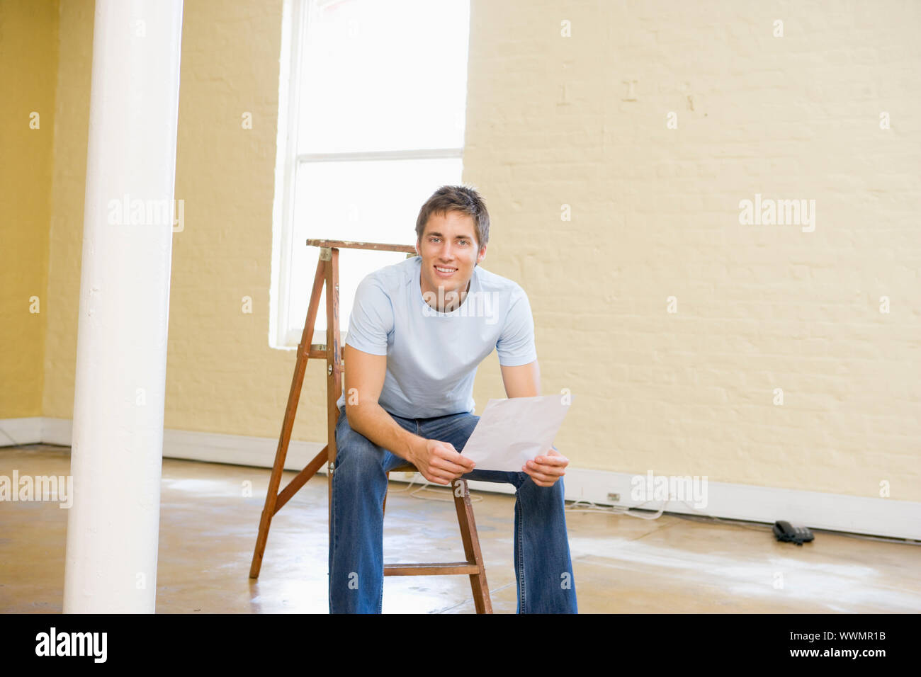 Man sitting on ladder in empty space holding paper smiling Stock Photo ...