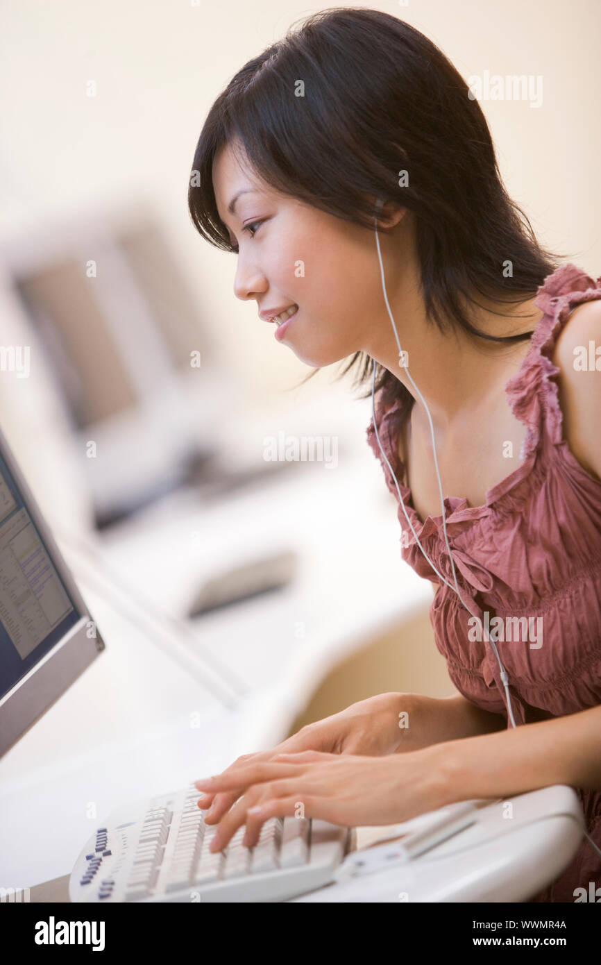 Woman in computer room listening to MP3 player while typing and Stock ...