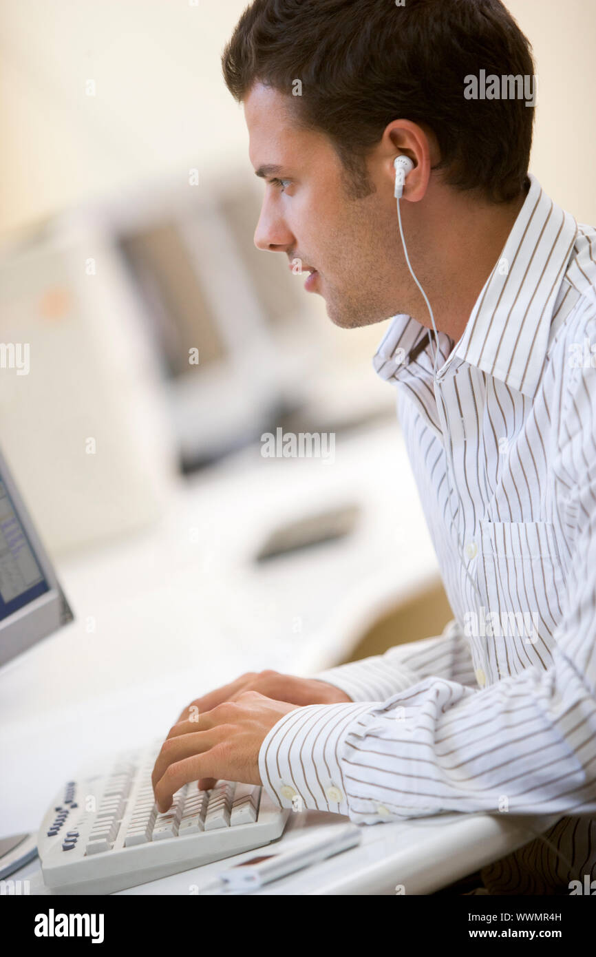 Man in computer room listening to MP3 player while typing Stock Photo ...
