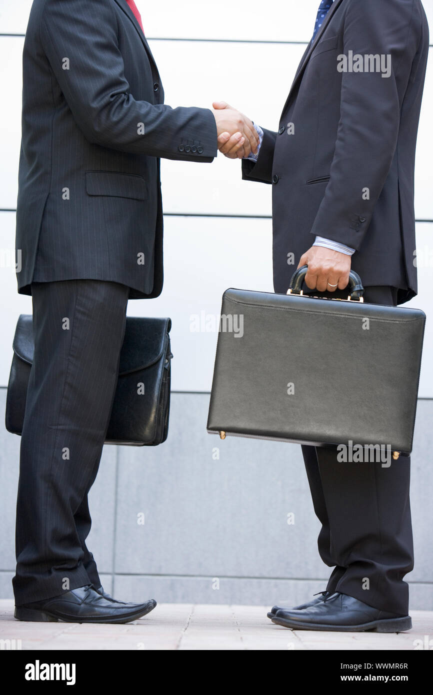 Two businessmen holding briefcases outdoors shaking hands Stock Photo ...
