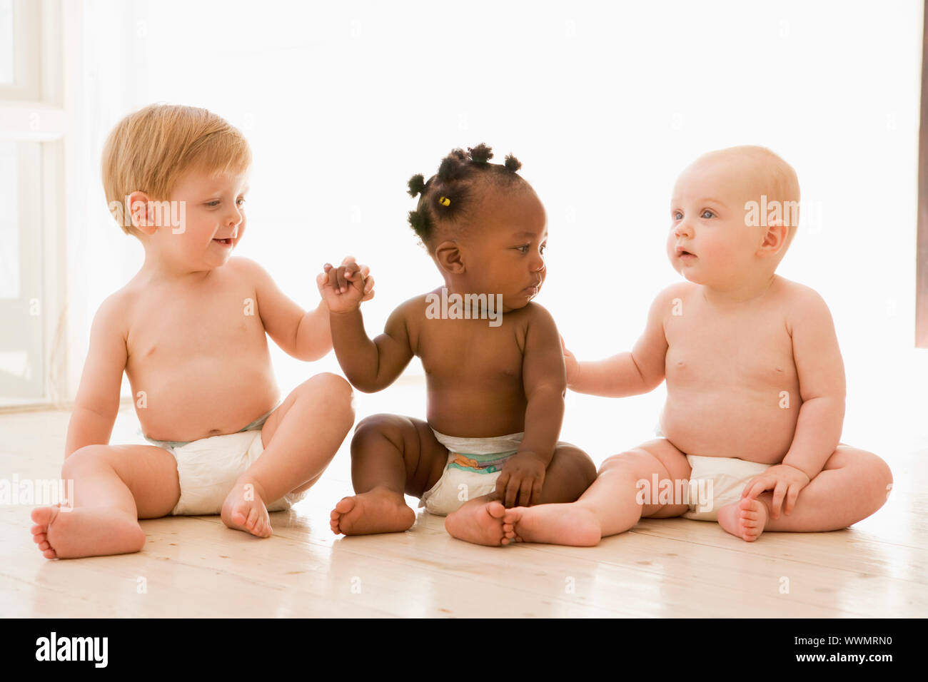 Three babies sitting indoors holding hands Stock Photo - Alamy