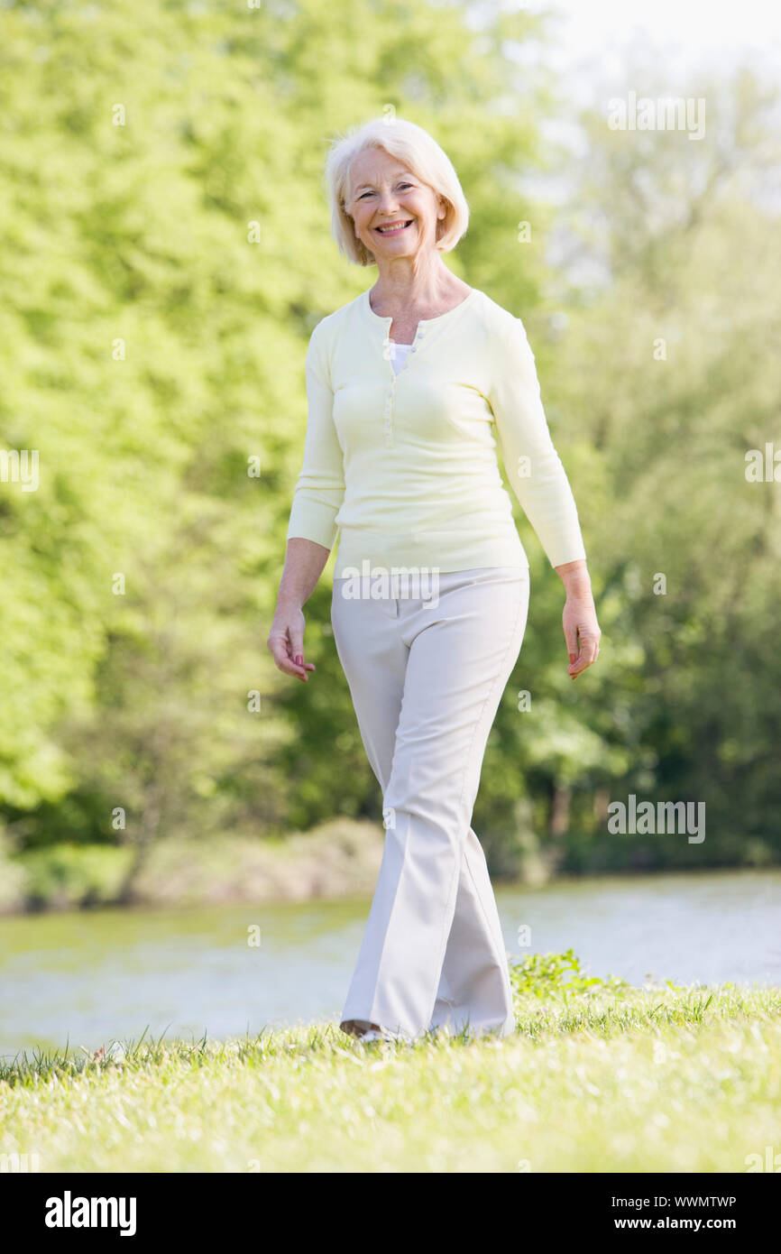 Woman walking outdoors at park by lake smiling Stock Photo - Alamy