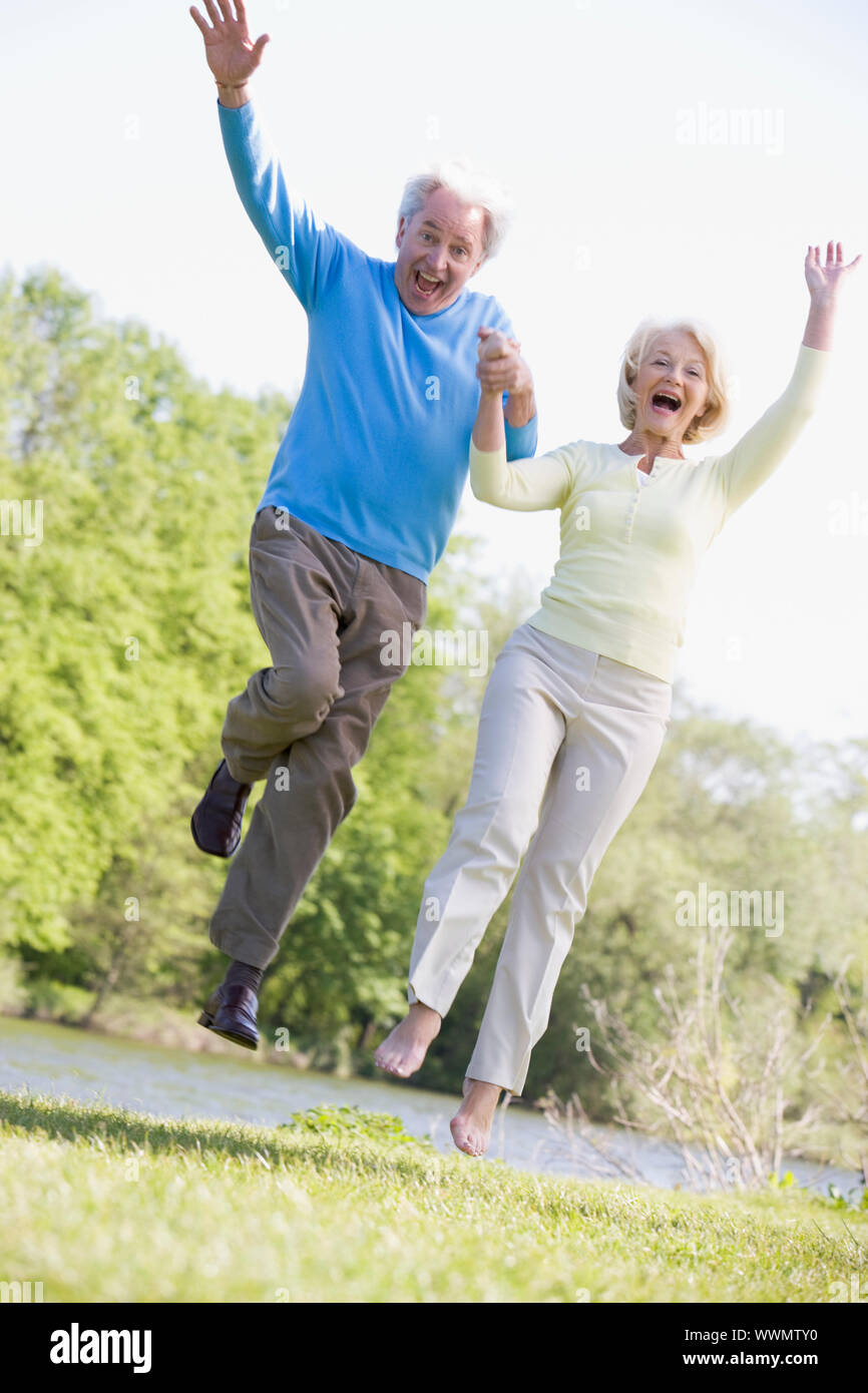 Couple jumping outdoors at park by lake smiling Stock Photo - Alamy