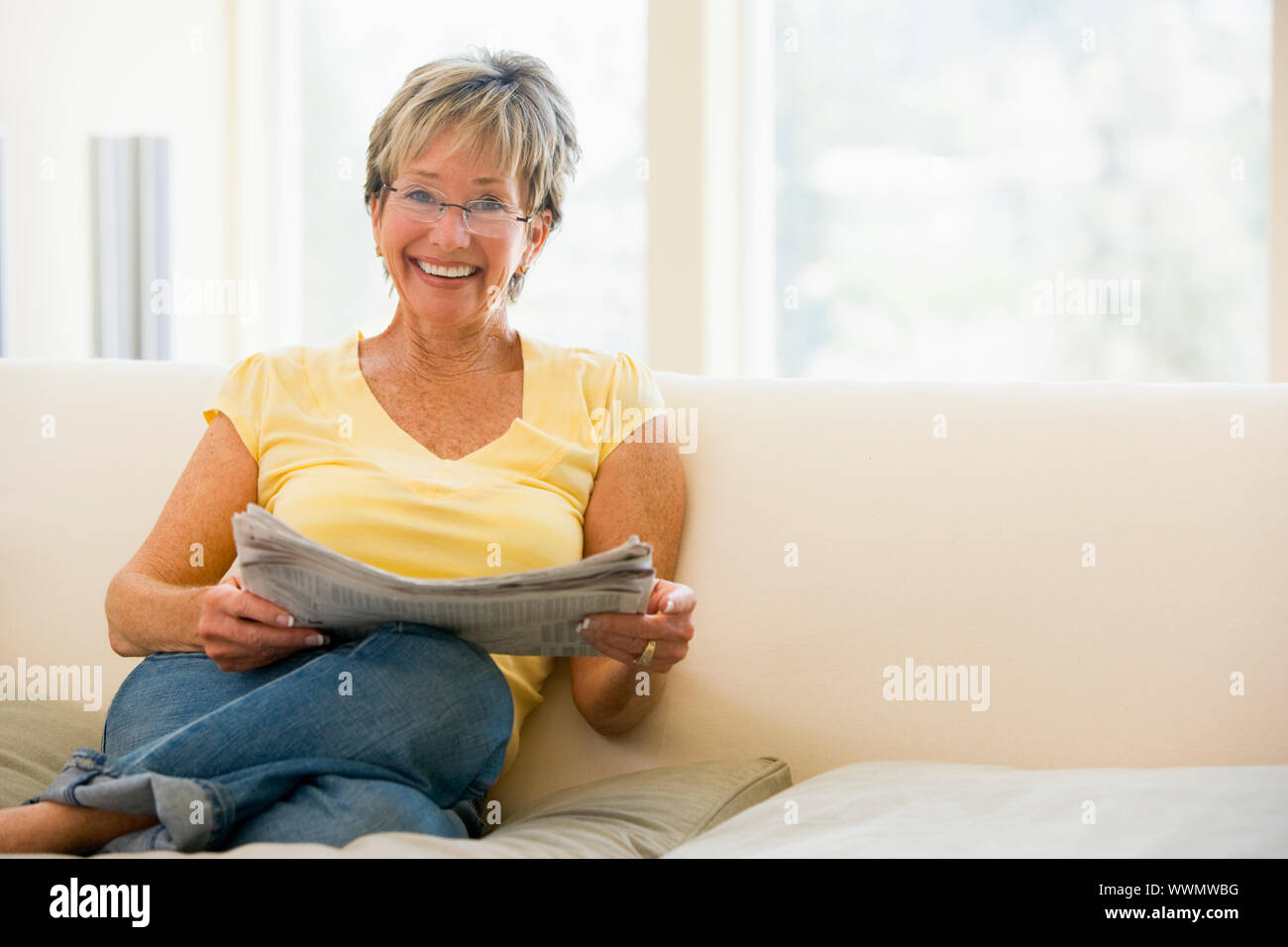 Woman in living room reading newspaper smiling Stock Photo - Alamy