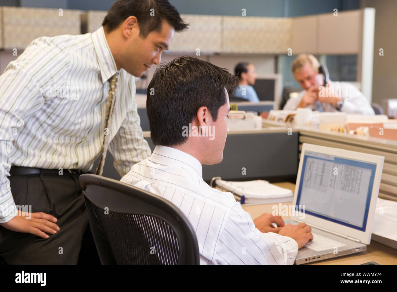 Two businessmen in cubicle looking at laptop Stock Photo - Alamy
