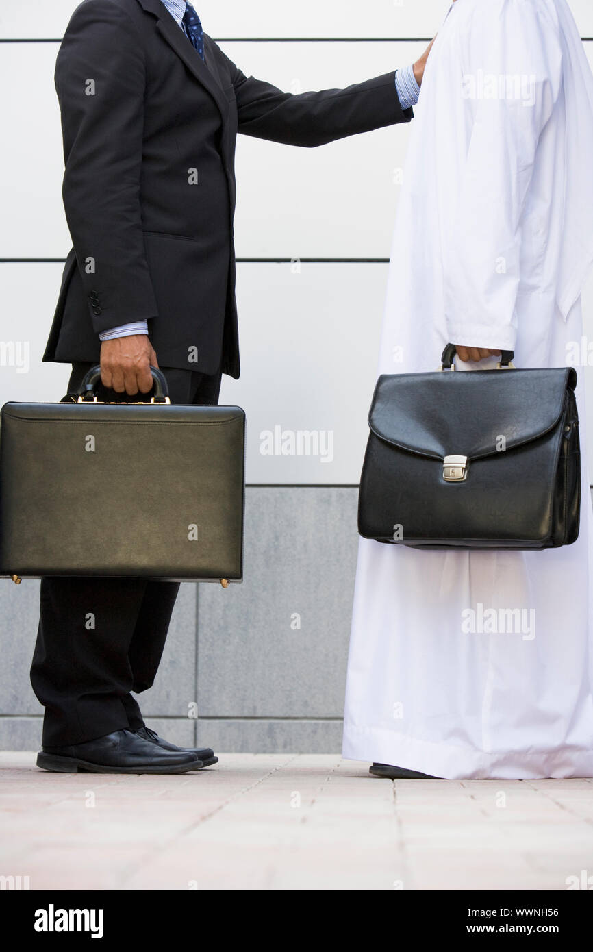 Two businesspeople standing outdoors with briefcases smiling Stock ...