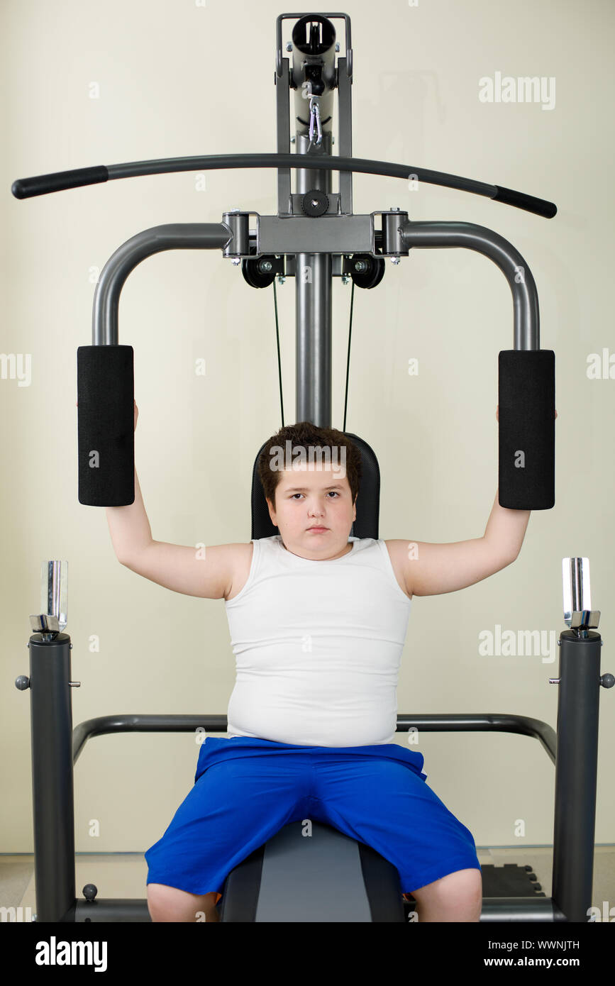 strong overweight little boy sitting on fitness equipment in gym during ...