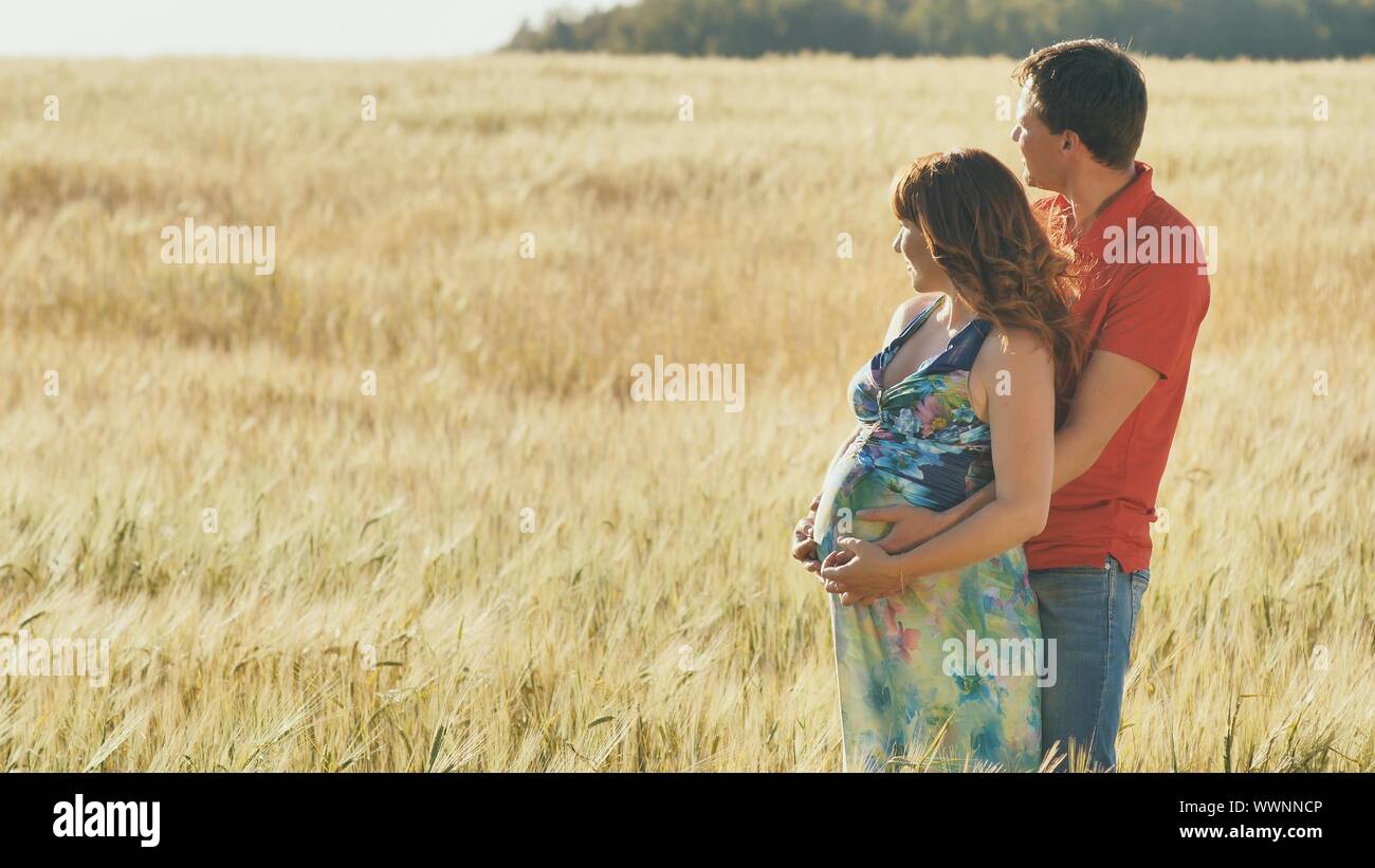 Pregnant woman and her husband hugging on the tummy together in nature ...