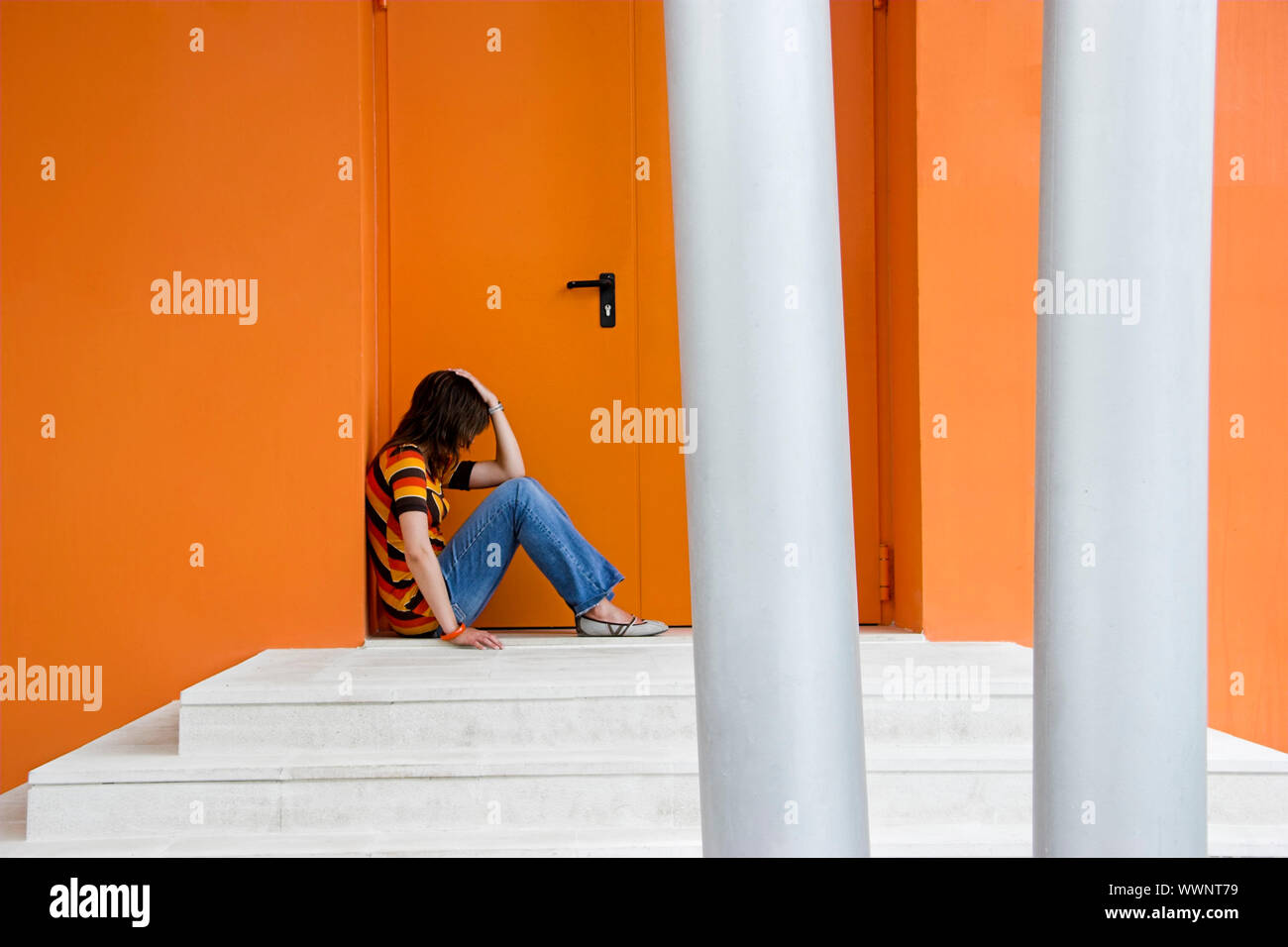 Loneliness woman on a orange door with hands over the knees Stock Photo ...