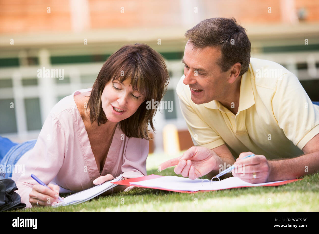 Adult students lying on lawn of school studying and talking Stock Photo ...