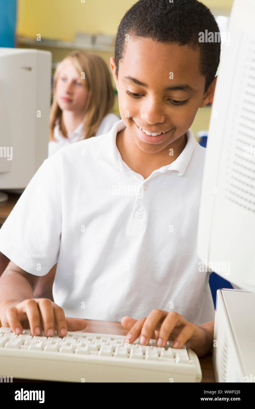 Student at computer terminal typing with student in background ...