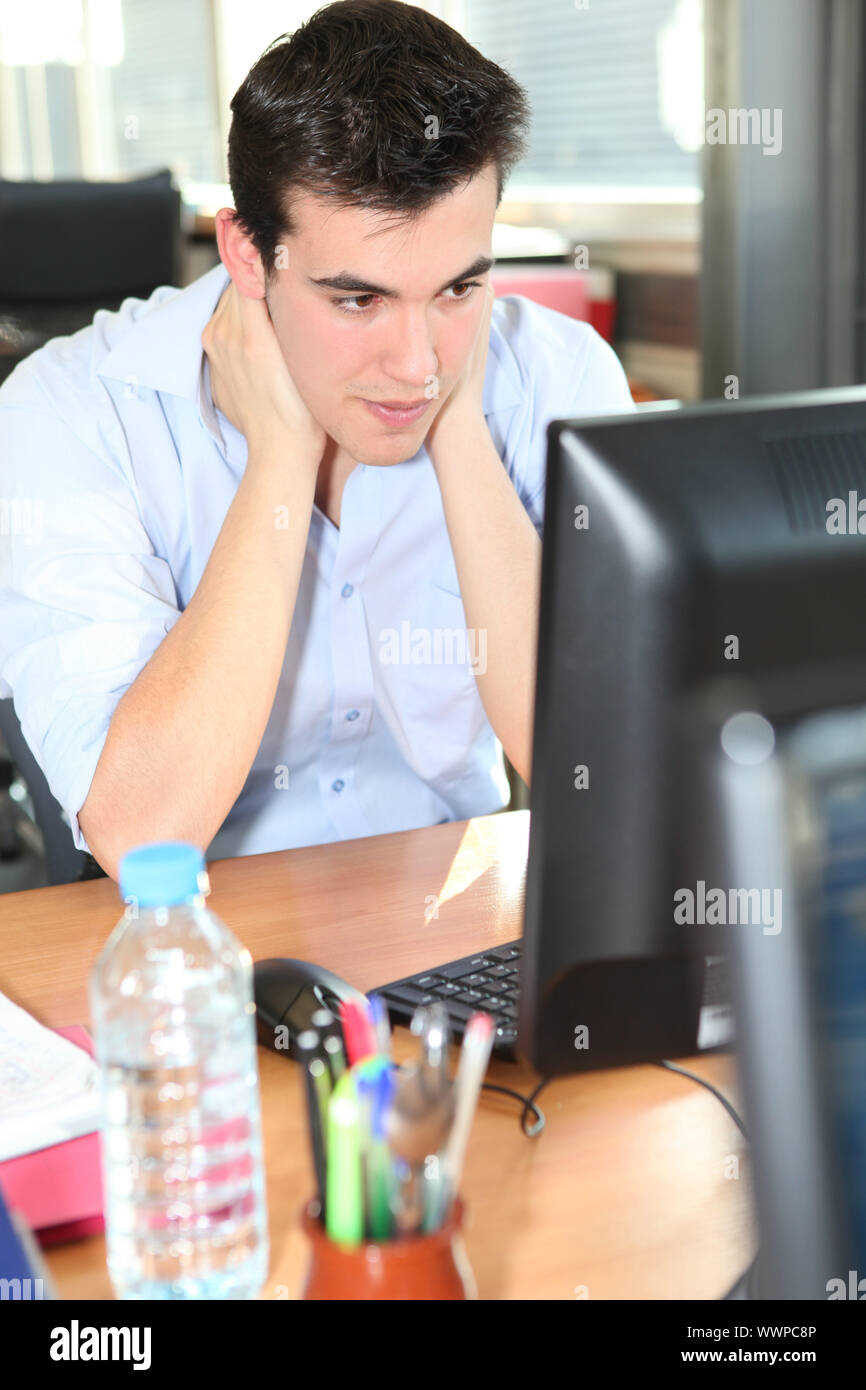 Young man holding his neck in front of a desktop computer Stock Photo ...