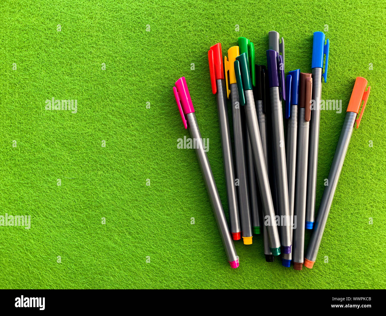 Top view, multi colored pens at green background Stock Photo - Alamy