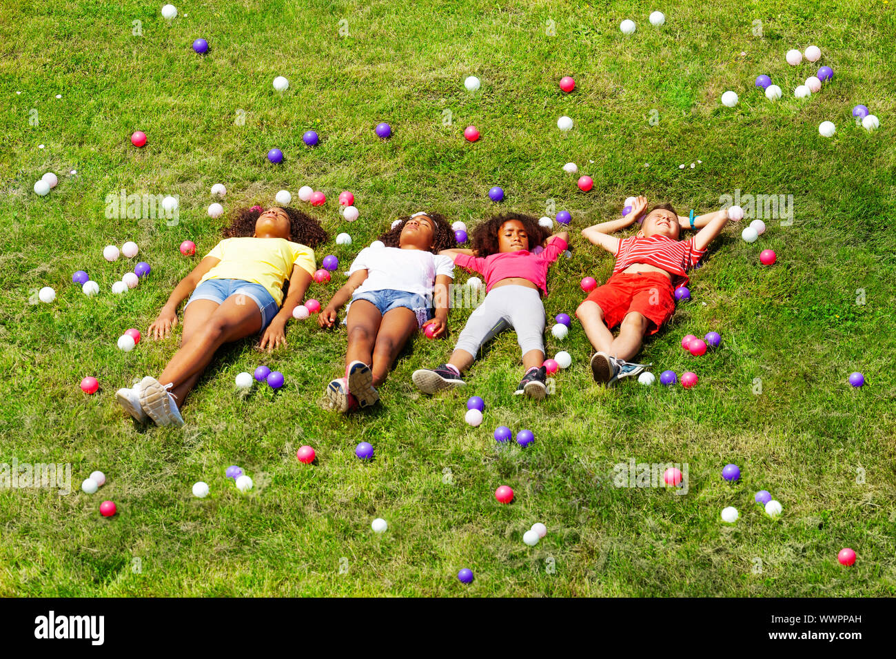 Kids lay in the grass and with color balls around Stock Photo - Alamy
