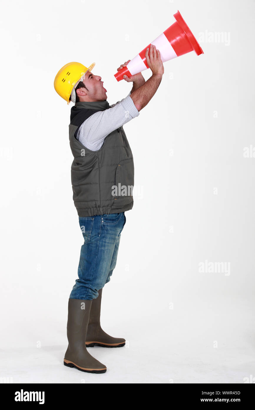 full-length picture of builder in profile shouting in construction cone ...