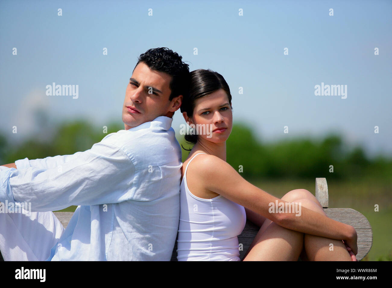 Young couple sat back to back on bench Stock Photo - Alamy