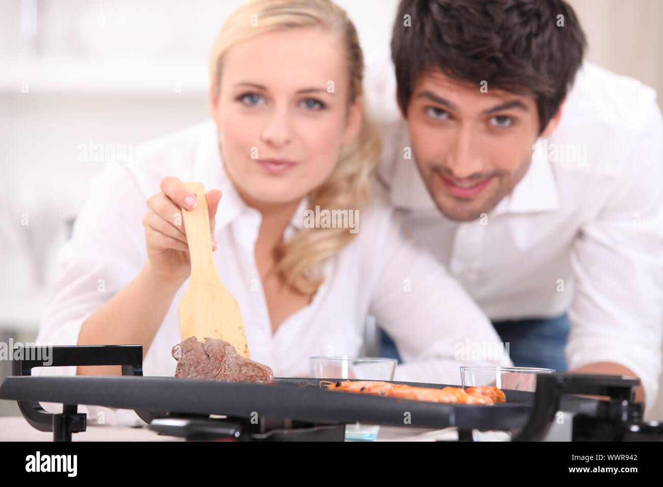a couple facing the camera and showing meat cooked on an electric ...