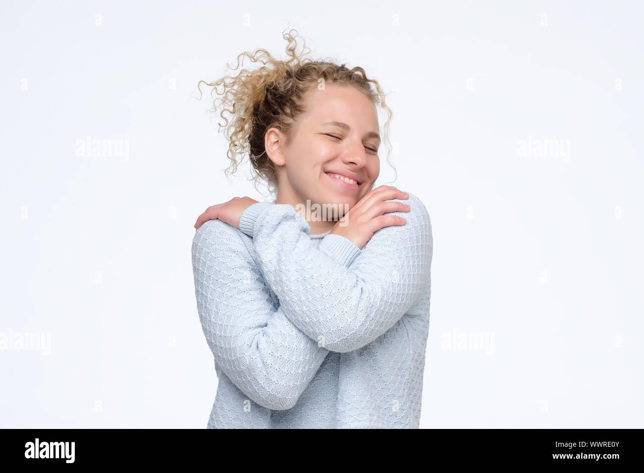 Attractive tender curly young woman standing and hugging herself over ...