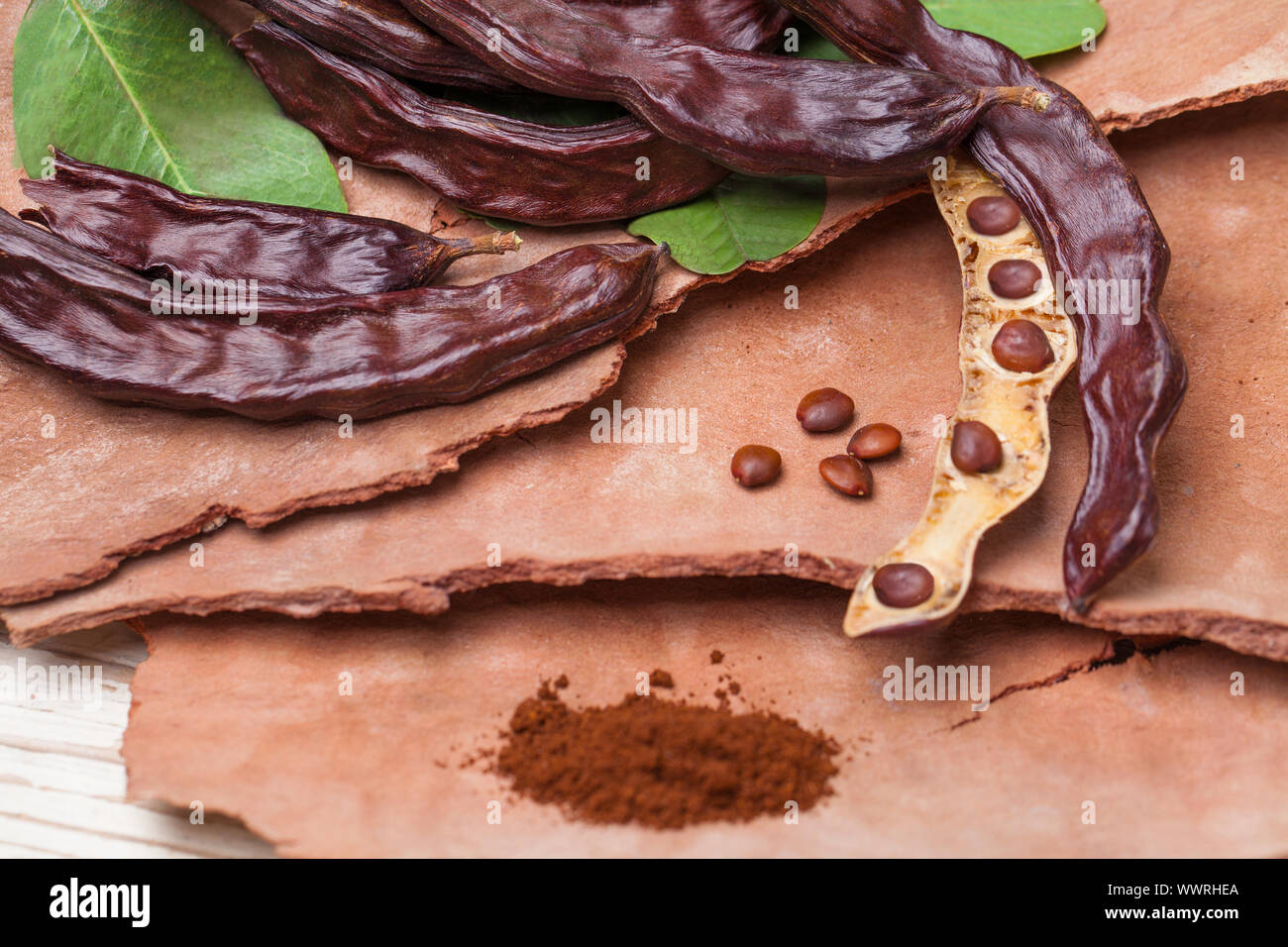 Carob. Organic carob pods with seeds and leaves on tree bark table ...