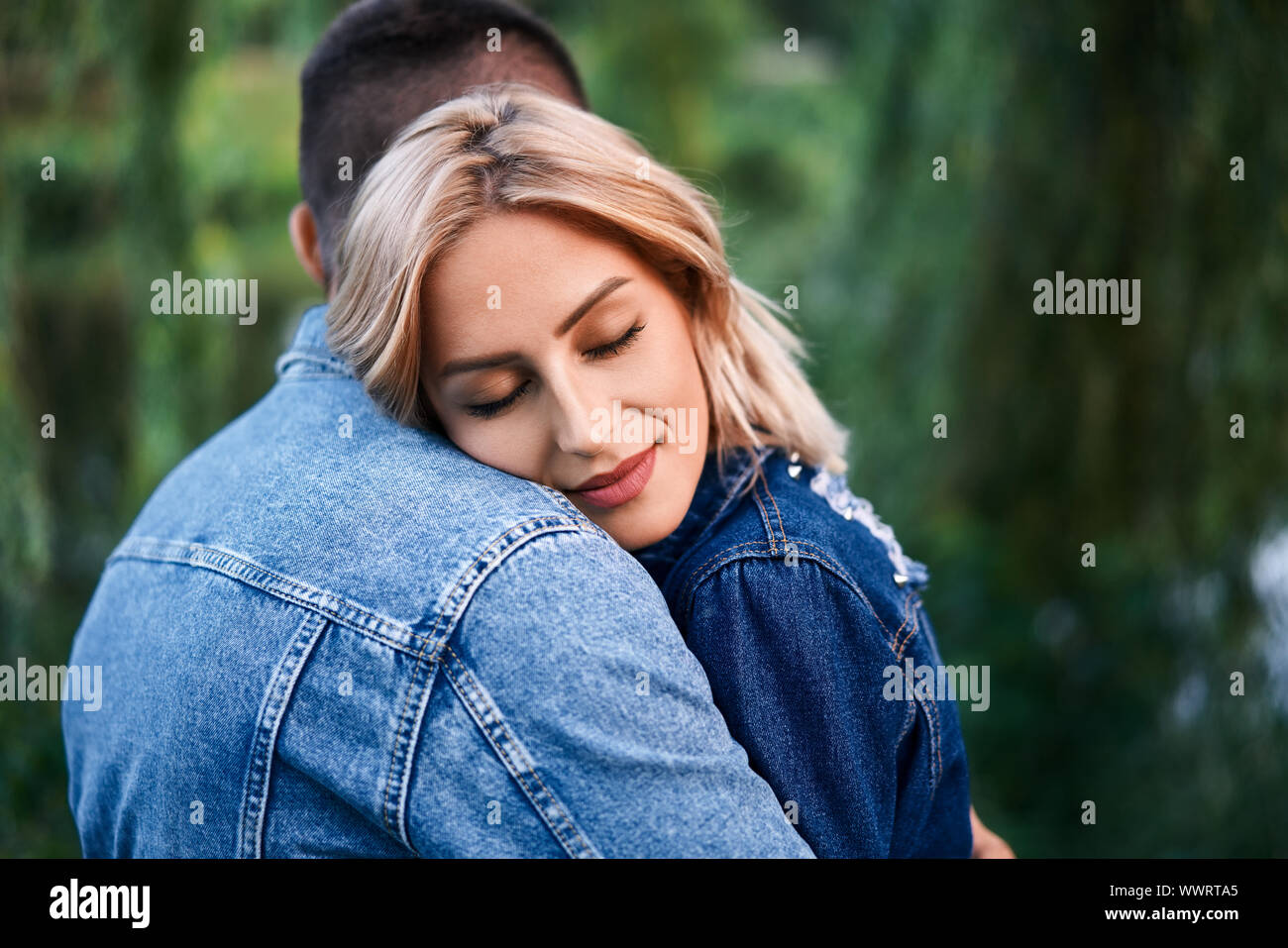 Young beautiful woman hugging her boyfriend with love outdoors. Caucasian couple in park ...