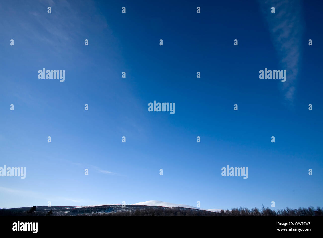 A deep blue sky background with faint clouds and a sliver of mountains ...