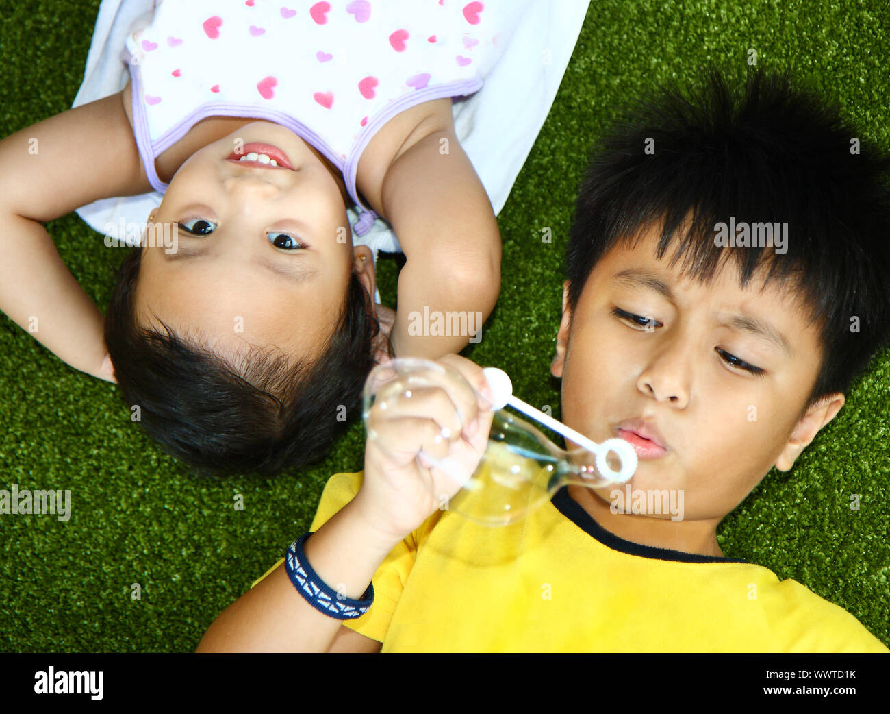 Two Kids Outside Lying And Playing On The Grass Stock Photo - Alamy