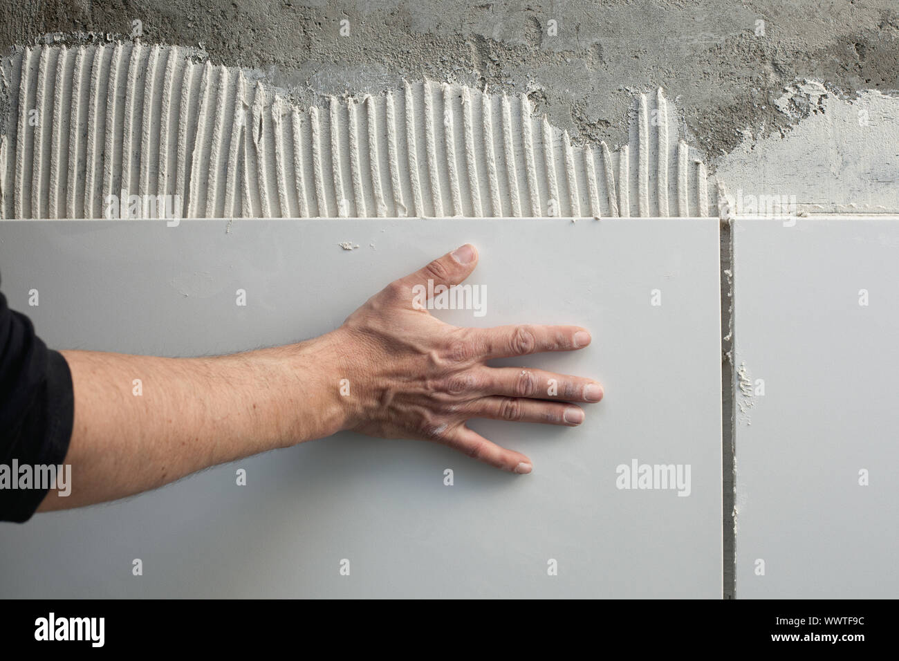 construction mason man hands on tiles work with notched trowel cement ...