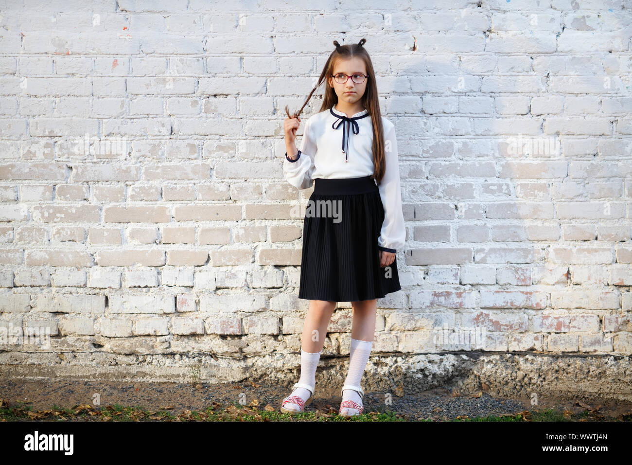 Schoolgirl standing against white brick wall background. Child girl in ...