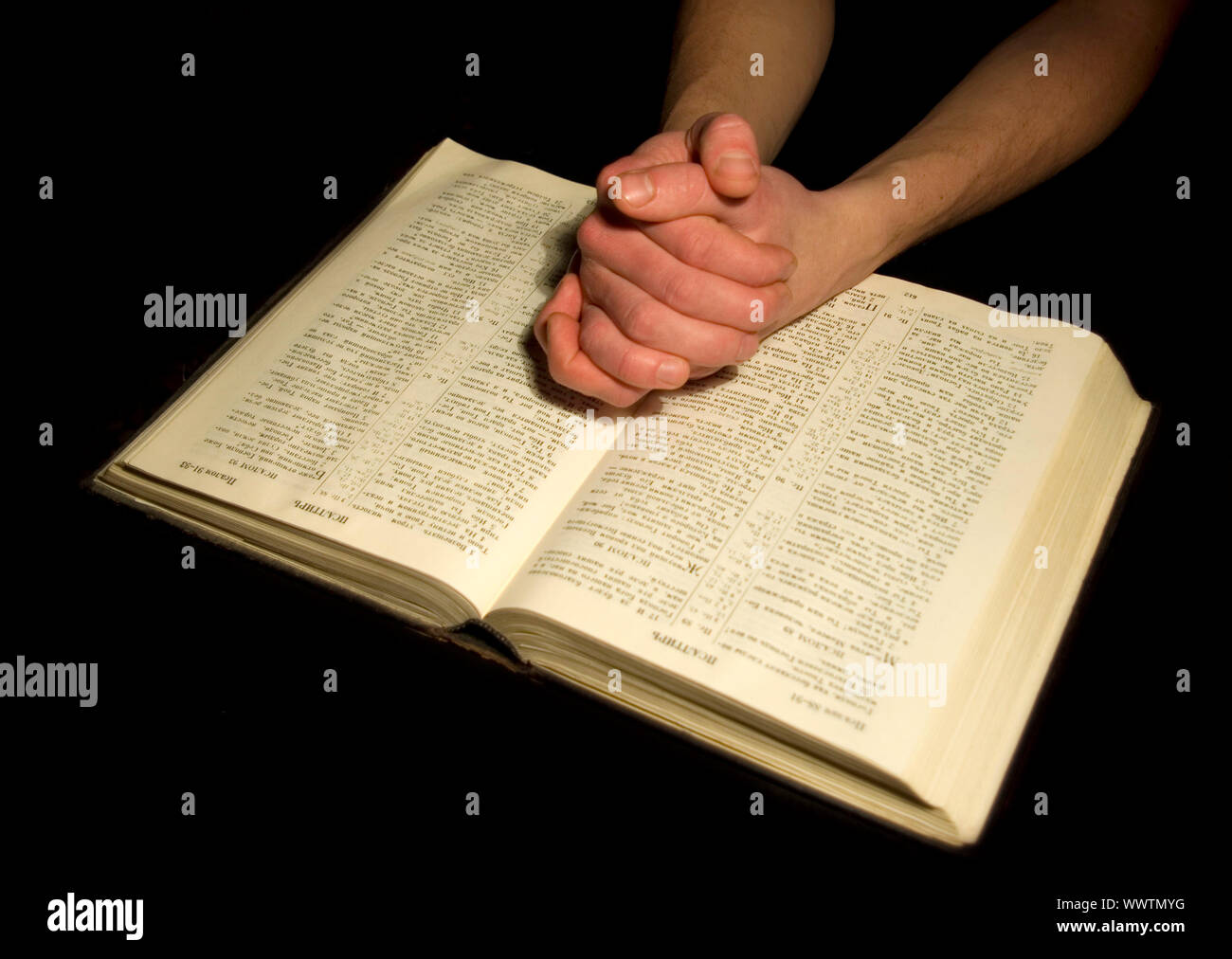 A mans hands clasped in prayer over a Bible Stock Photo - Alamy