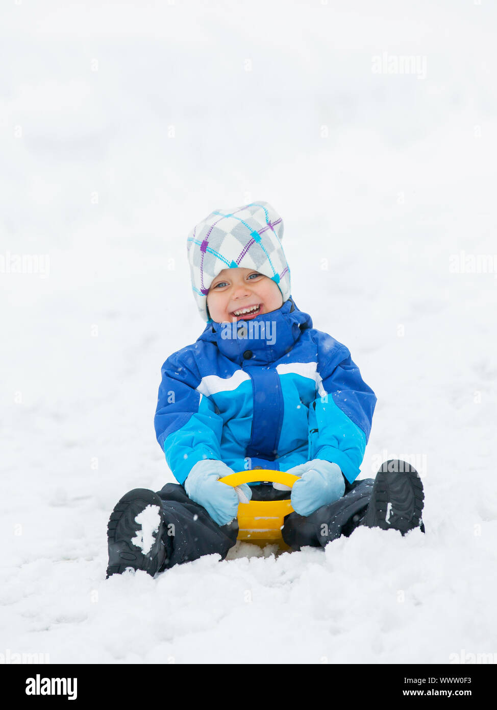 Cute little boy in blue riding on a sled near the Austrian cottage ...