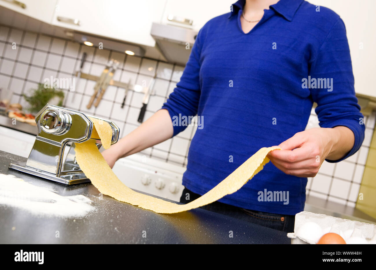 A young female stretching out pasta over the counter from a manual ...