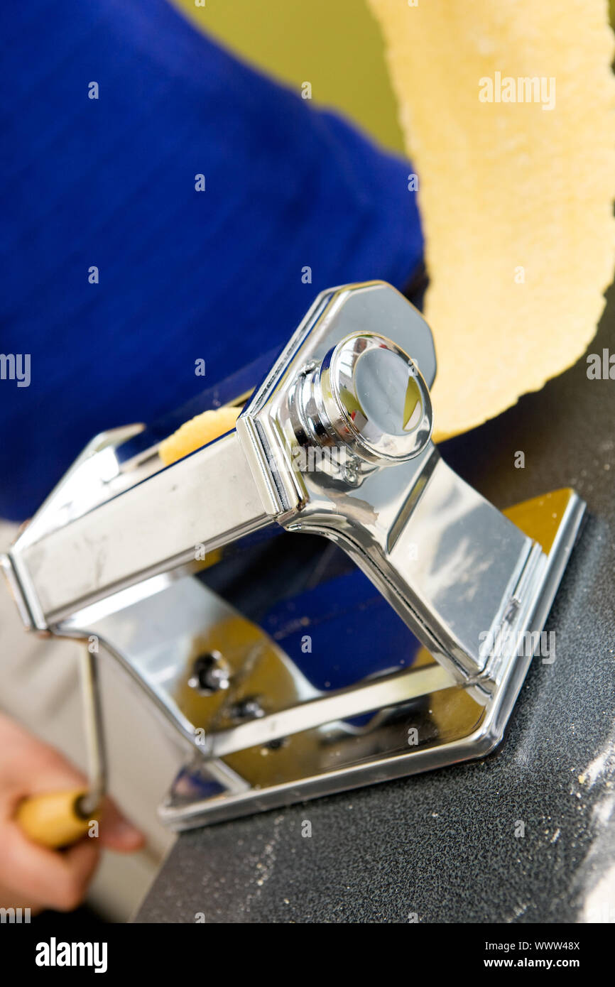A young female stretching out pasta over the counter from a manual ...