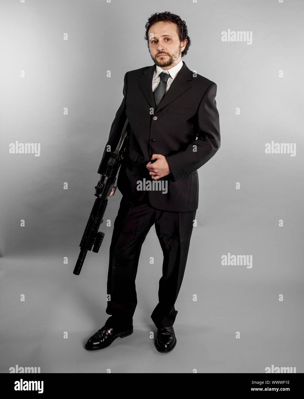 Businessman in black suit and armed with machine gun on gray background ...