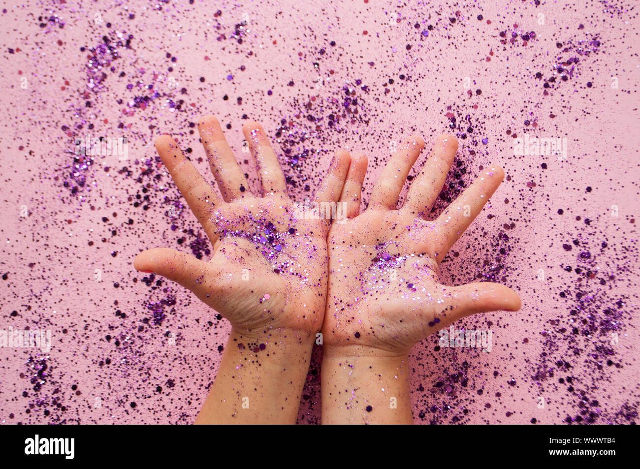 Child's hands with purple color sparkles on pastel pink background ...