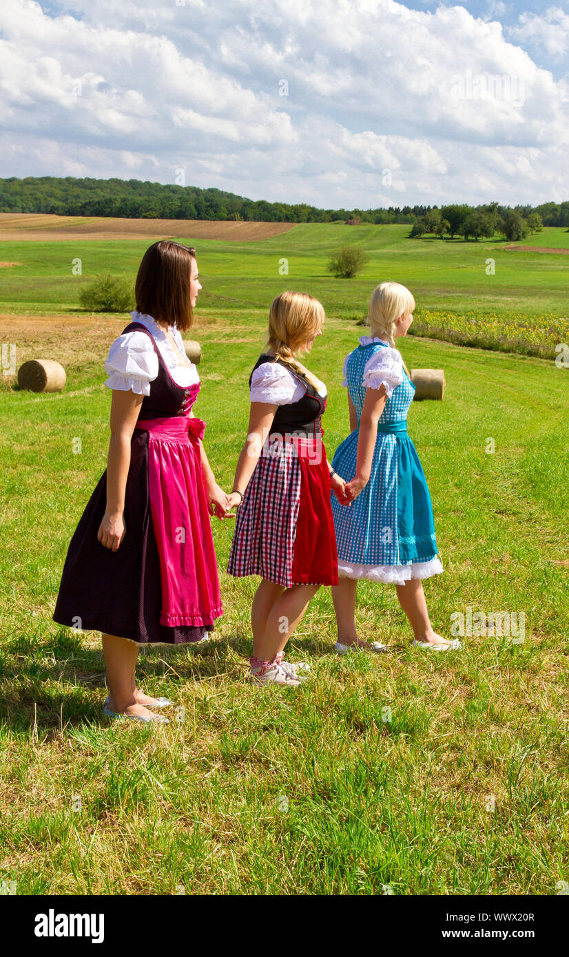 Three girls in colorful dirndls walking hand in hand on a meadow Stock ...