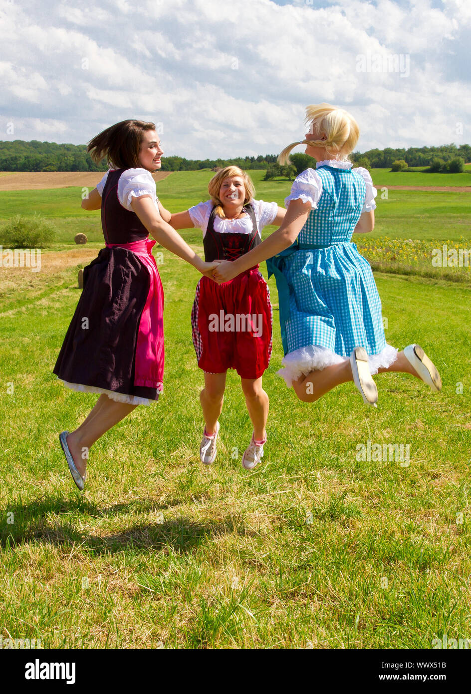 Three happy girls in colorful dirndl jump up in the air Stock Photo - Alamy