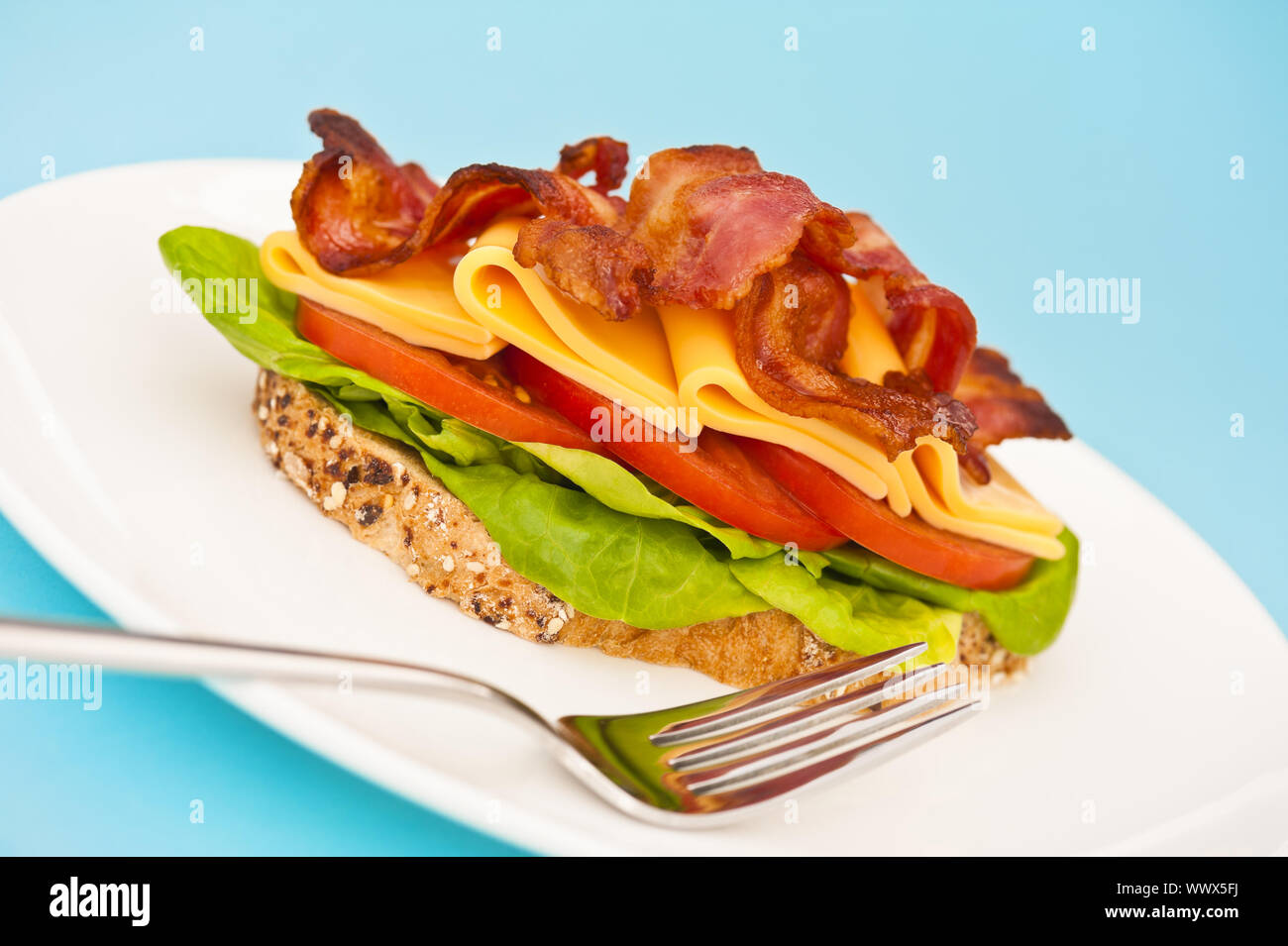Open blt sandwich on a white plate with blue background and fork Stock ...